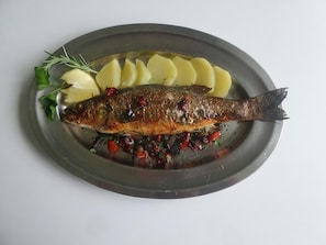 Um peixe inteiro grelhado com fatias de limão e ervas sobre um prato.