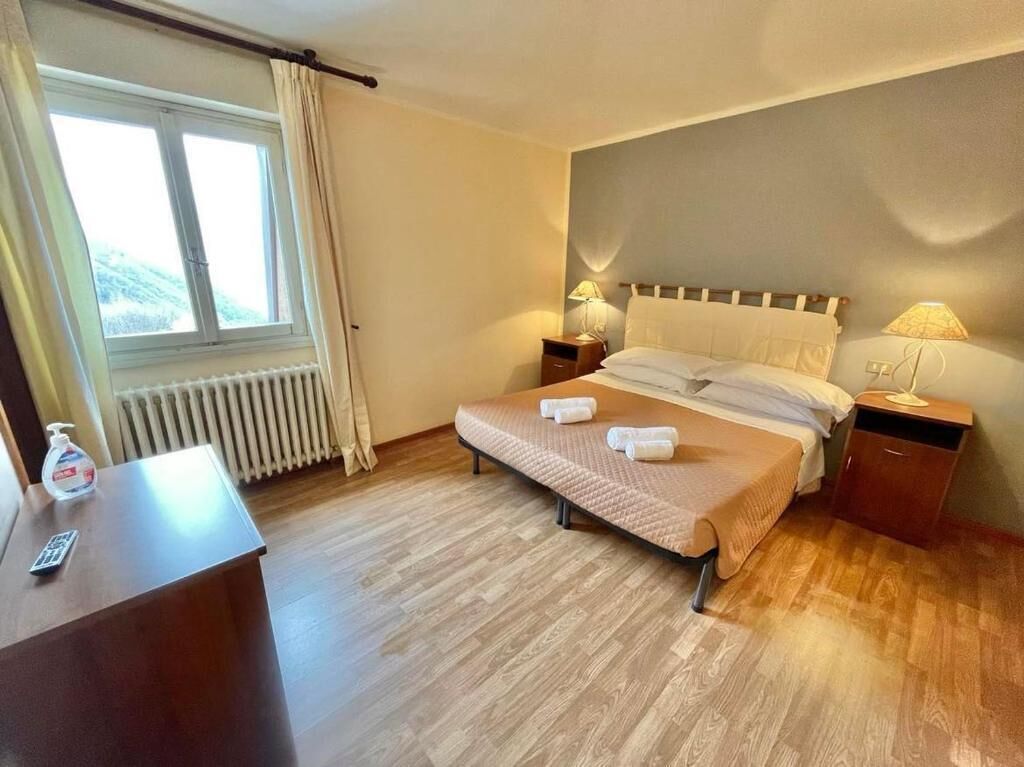 Quarto de hotel com cama, mesas de cabeceira, janela e radiador.