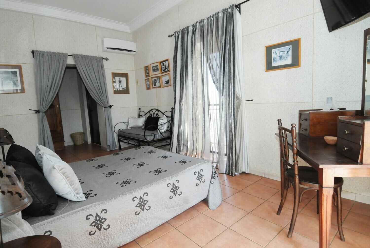 Quarto com cama, escrivaninha, cadeira e janela com cortinas.