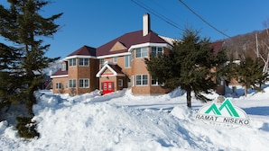 Um edifício grande de tijolos com uma porta vermelha e várias janelas, rodeado por neve.