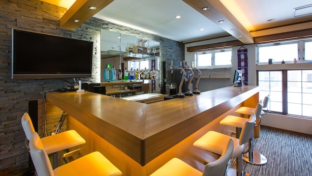 Uma área de bar com um balcão comprido, vários banquetes, uma televisão de tela plana e uma parede de pedra.