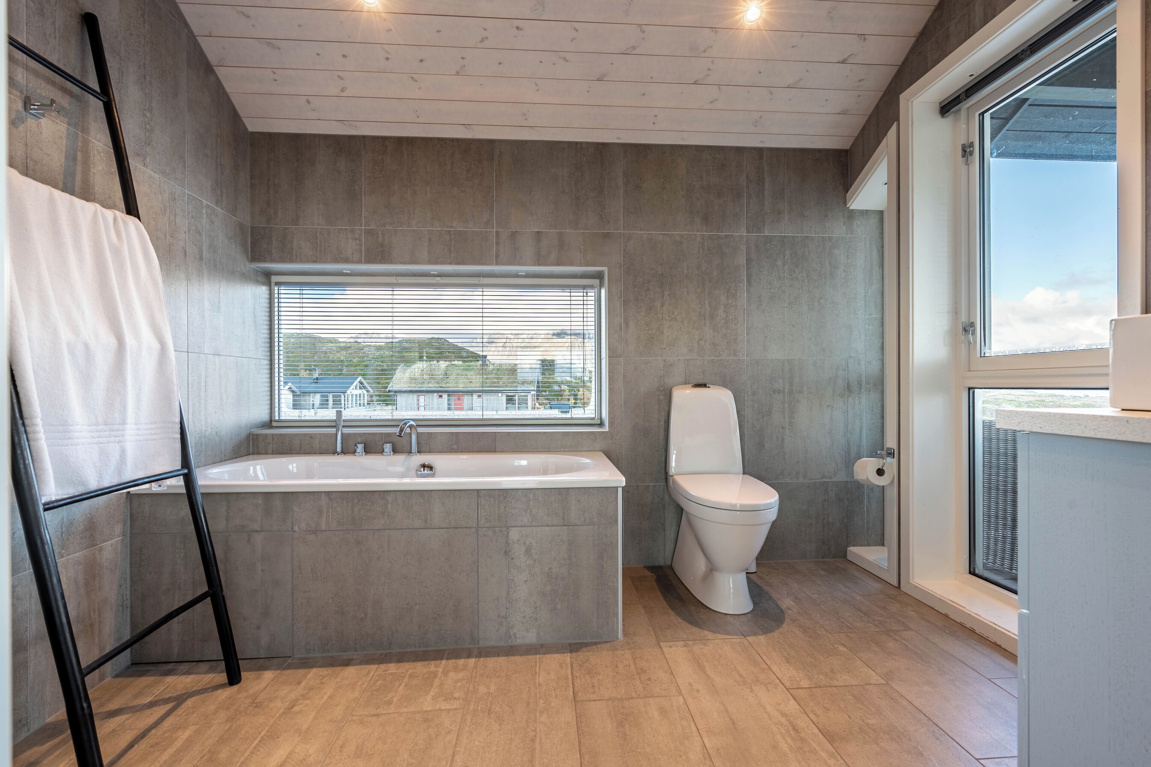Uma casa de banho moderna com banheira, sanita e janela ampla.