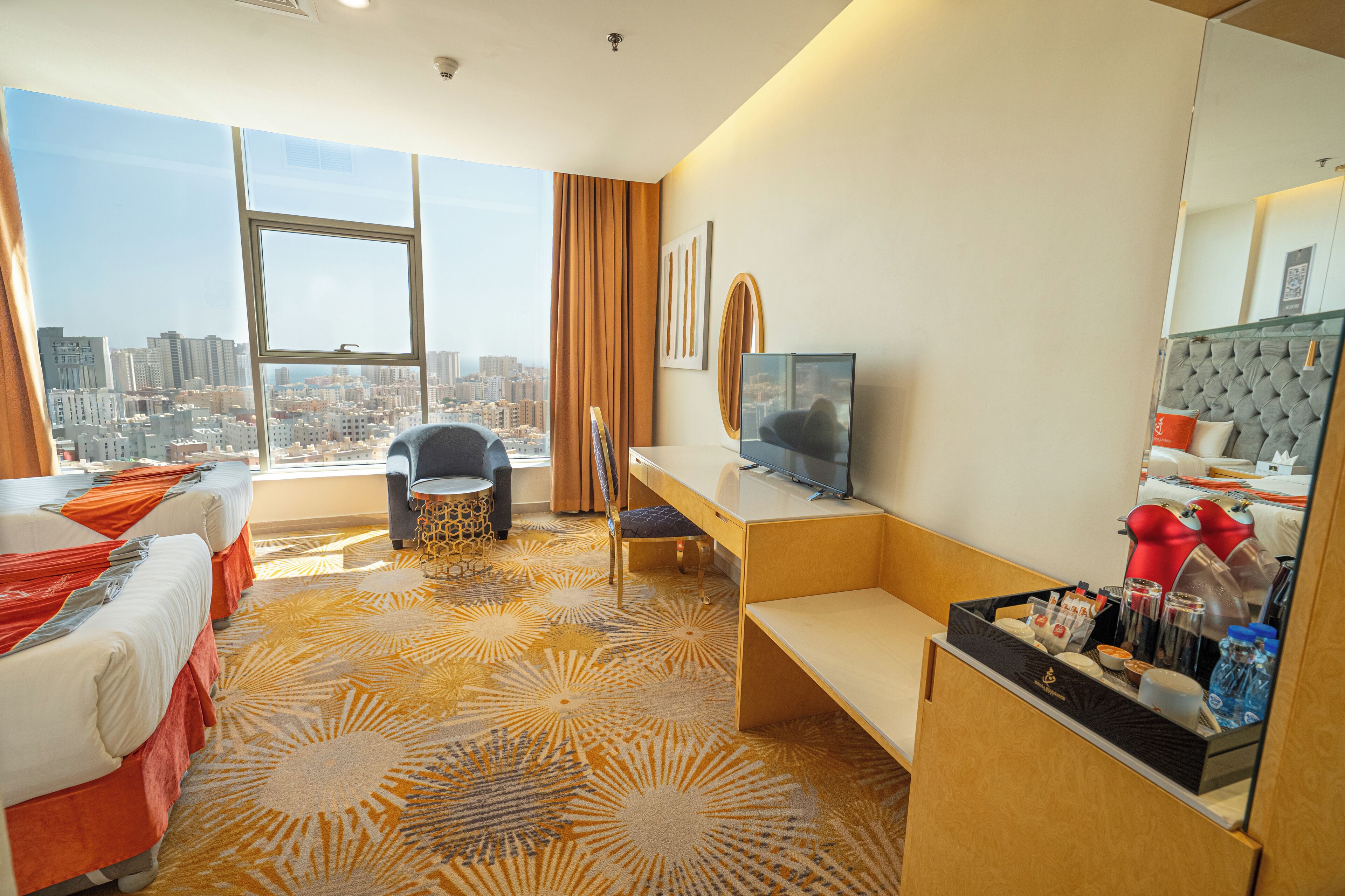 Quarto de hotel com vista para a cidade, uma cama, uma secretária com televisão, uma cadeira e uma pequena mesa com comodidades.