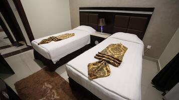 Quarto de hotel com duas camas de solteiro, um tapete marrom, uma mesa de cabeceira com abajur e uma cabeceira escura.