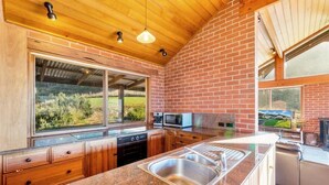 Cozinha com bancadas de granito, eletrodomésticos de aço inoxidável e uma janela grande com vista para uma paisagem verdejante.