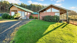 Uma casa moderna de dois andares com telhado verde, varanda coberta e gramado bem cuidado.
