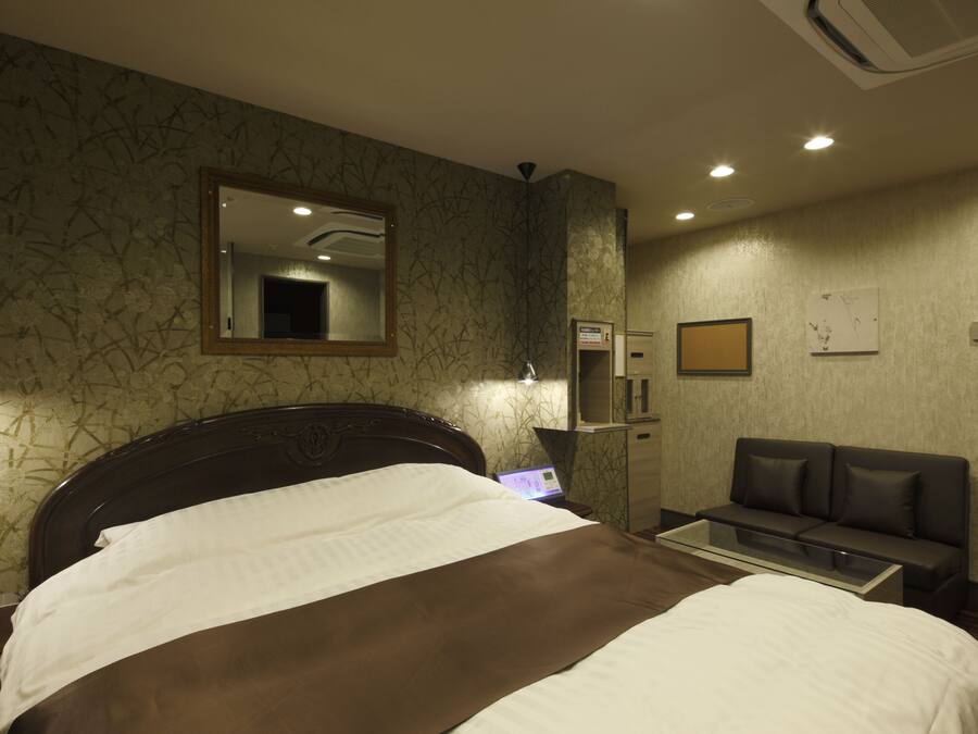 Quarto de hotel com cama, escrivaninha, sofá, espelho e parede com textura.