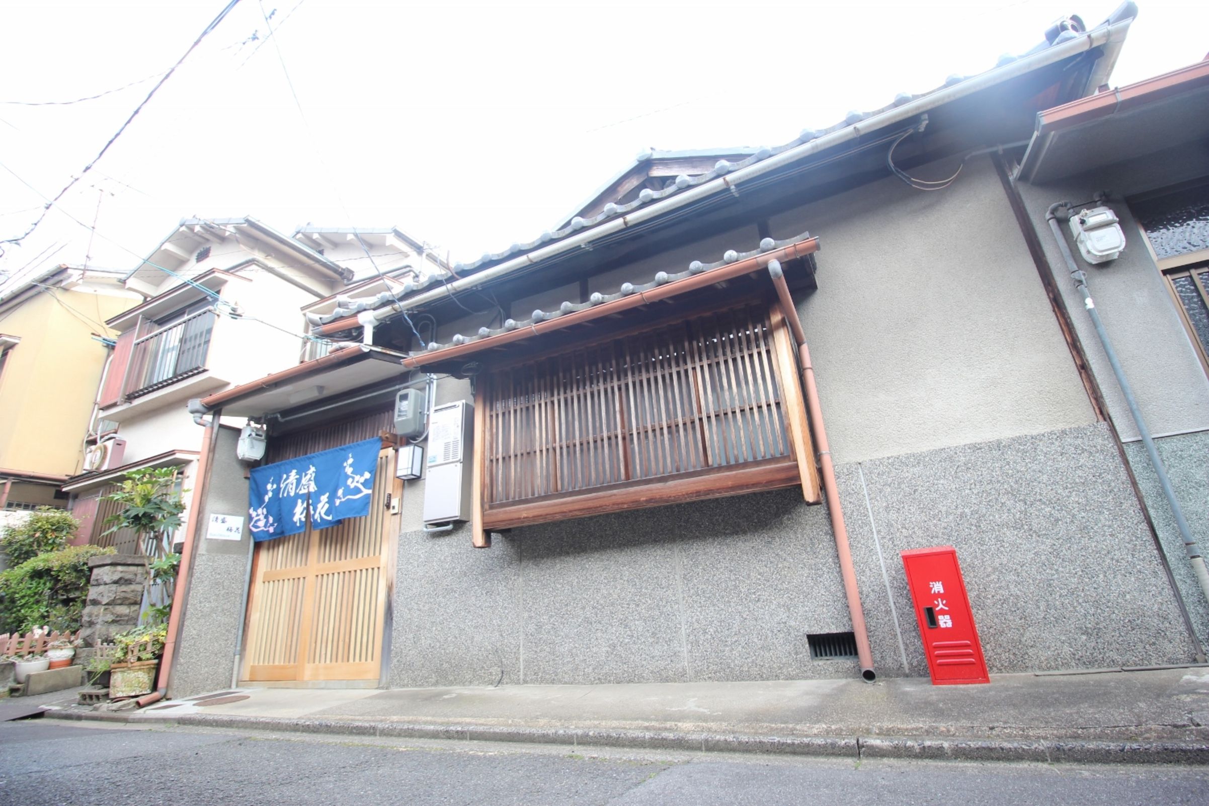 Um edifício tradicional japonês com portão de madeira, placa azul e caixa de correio vermelha.