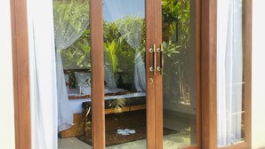 Uma porta de correr de vidro com vista para uma cama e uma pequena mesa com uma planta.