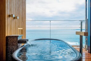 Banheira de hidromassagem com vista para o oceano, painéis de madeira e guarda-corpo de vidro.