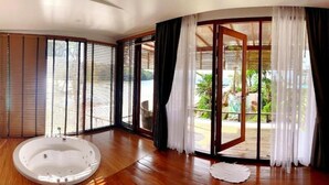 Um quarto com uma banheira grande, portas de vidro deslizantes que dão para uma varanda e piso de madeira.