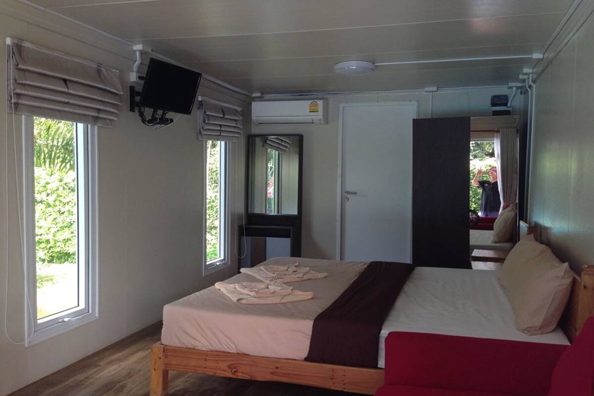 Quarto com cama, televisão fixada na parede e janela com persianas.