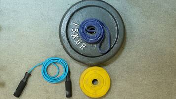 Um disco de haltere com a inscrição 15KG, uma corda de pular azul, um disco de peso amarelo e uma barra de metal.