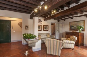Uma sala de estar acolhedora com lareira de pedra, poltronas listradas, um aparador de madeira e uma escadaria que sobe.