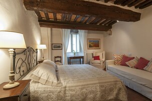 Quarto com cama, mesa de cabeceira com abajur, poltrona, sofá e janela com cortinas.