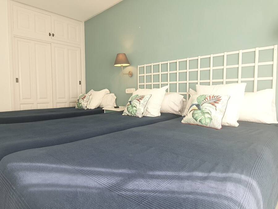 Quarto com duas camas, um guarda-roupa branco, uma mesa de cabeceira e uma luminária na parede.
