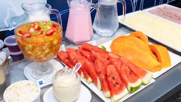 Uma mesa de buffet com diversos alimentos, incluindo salada de frutas, fatias de melancia e um jarro de água.