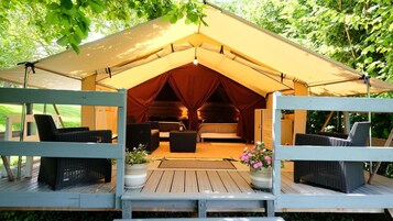 Acolhimento em tenda confortável com deck de madeira, móveis de vime e área de estar central.