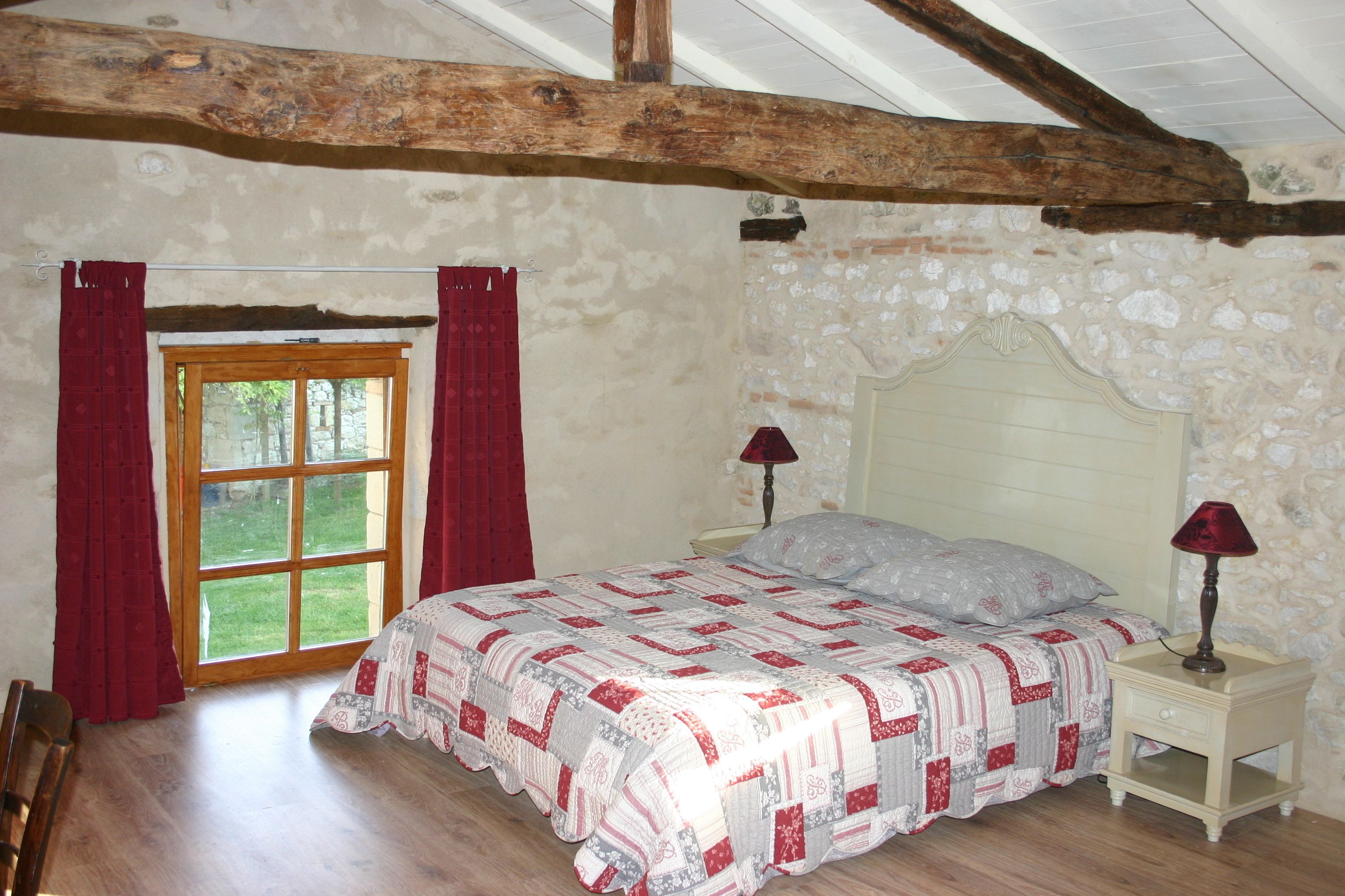 Quarto com cama de madeira, mesa de cabeceira, janela com cortinas e parede de pedra.