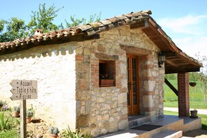 Um edifício de pedra com telhado ladrilhado, porta de madeira e placa indicando o caminho para a recepção, sala de jantar e piscina.