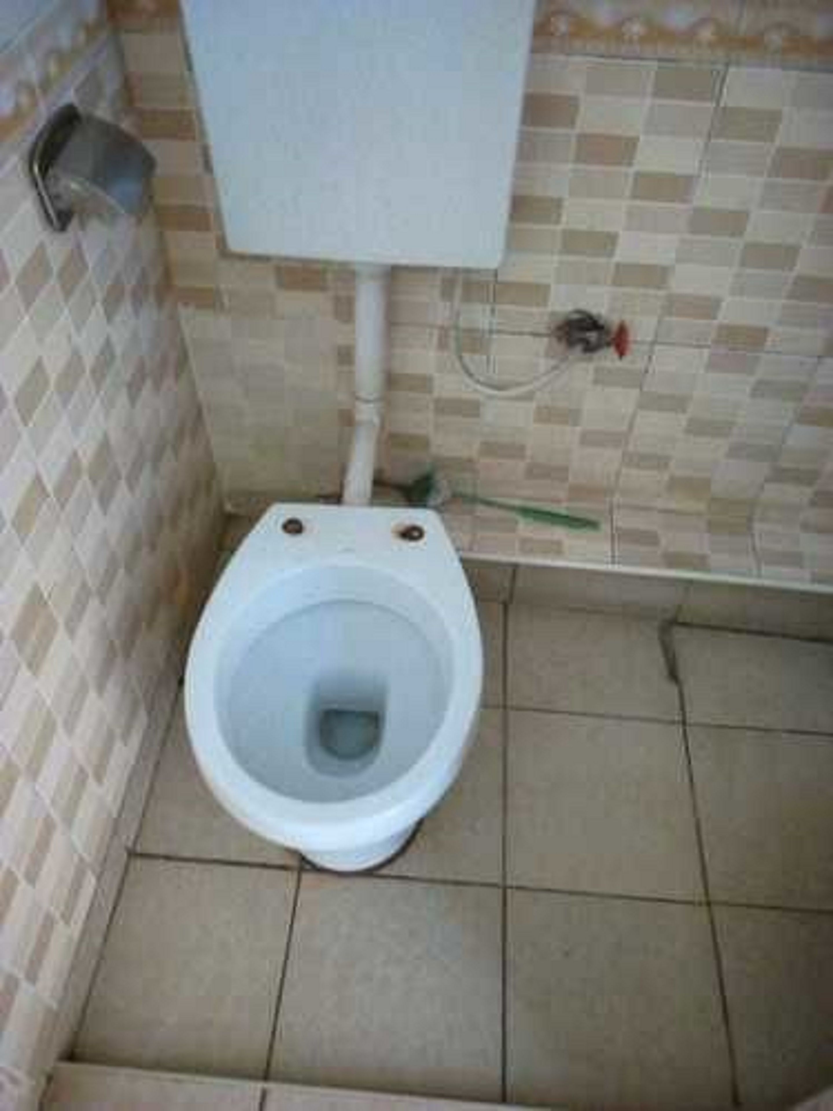 Um banheiro pequeno, com azulejos, contendo um vaso sanitário, um secador de mãos e um suporte de papel higiênico fixado na parede.