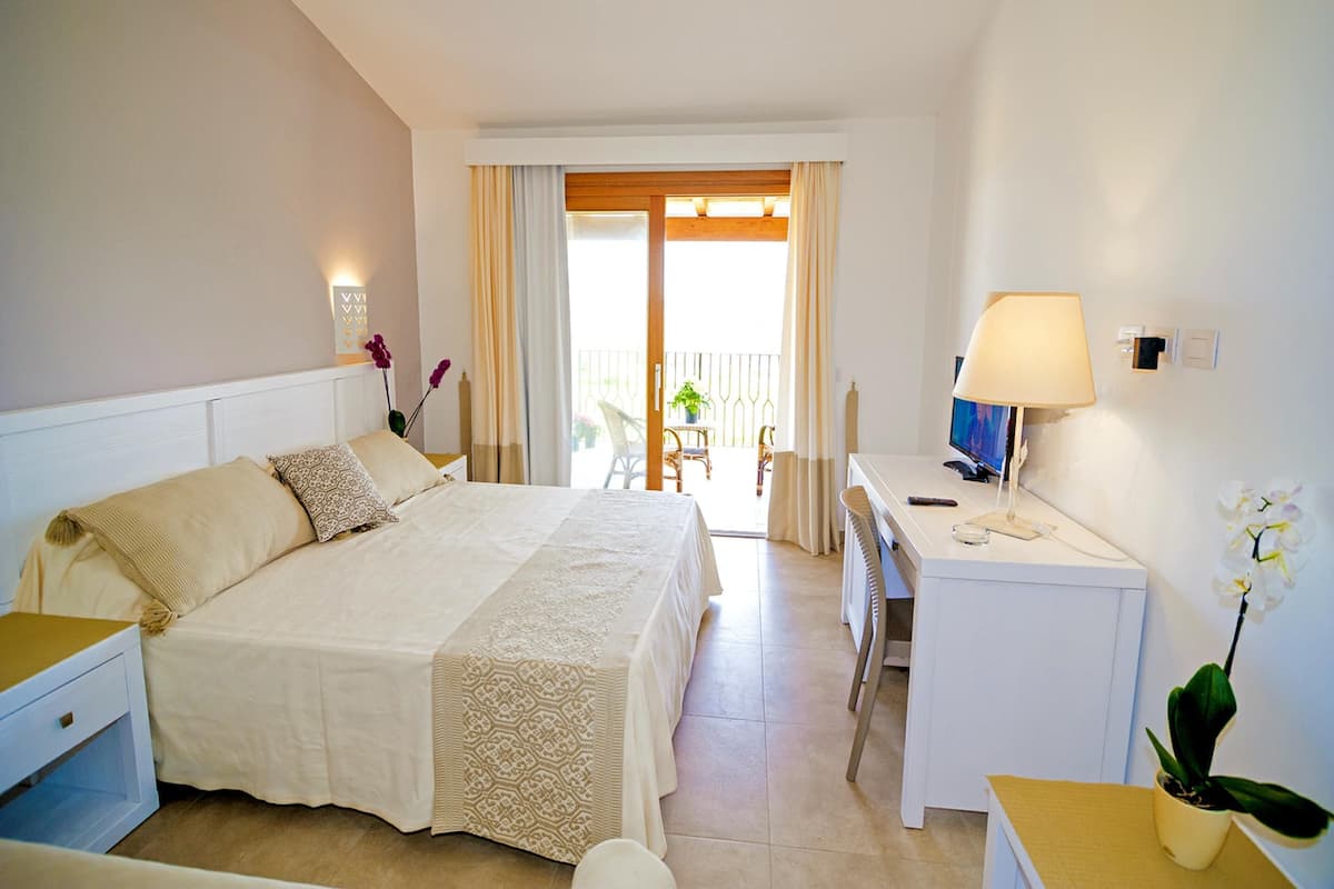Quarto de hotel com cama, escrivaninha, cadeira e varanda com mobiliário.