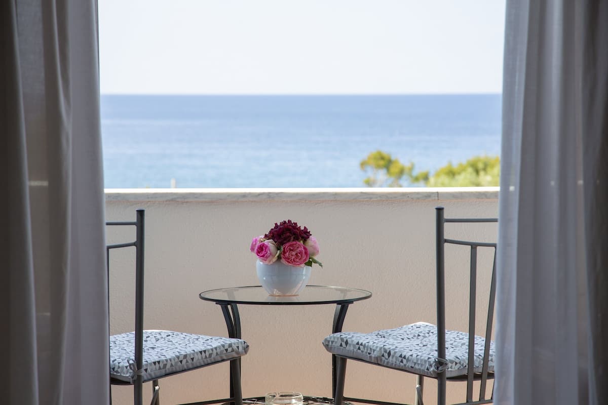 Varanda com mesa e duas cadeiras, um vaso com flores e vista para o mar.