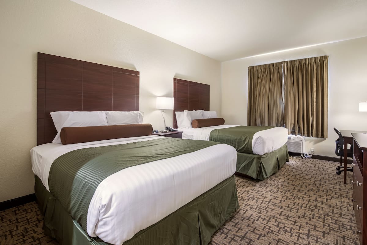 Quarto de hotel com duas camas, uma escrivaninha, uma cadeira e uma janela com cortinas.