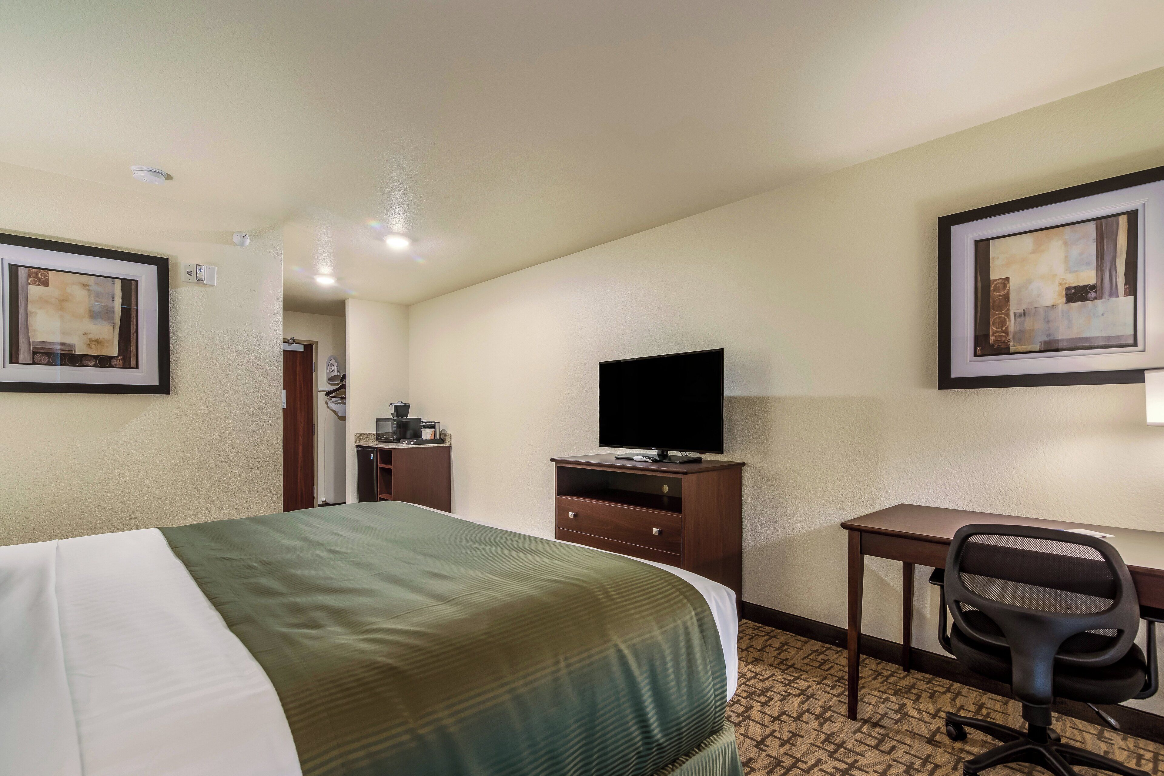 Quarto de hotel com cama, escrivaninha, cadeira, televisão e obras de arte nas paredes.
