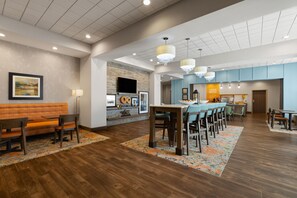 Um lobby de hotel moderno com área de estar, bar e cozinha ao fundo.