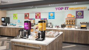 Espaço de café da manhã com estação de café, iogurte, aveia e opções de frutas.