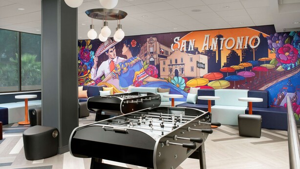 Mesa de futebol de mesa em área de lounge moderna, com um mural de San Antonio ao fundo.