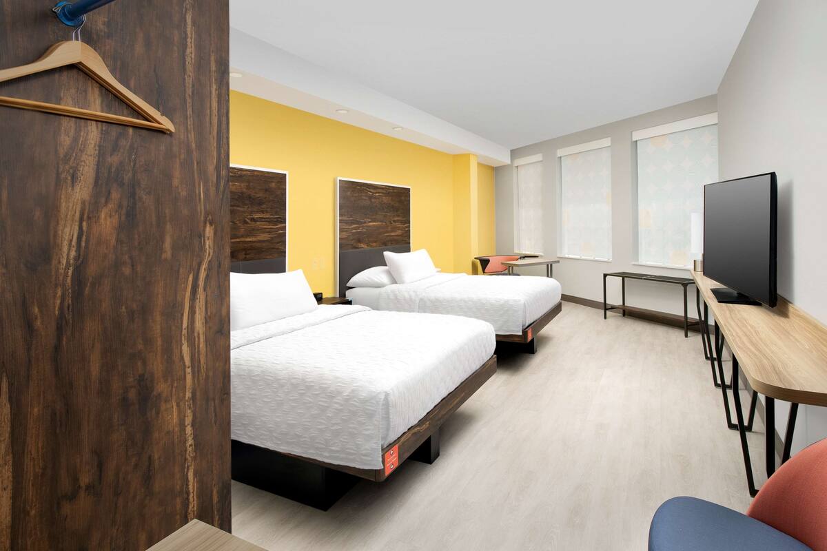 Quarto de hotel com duas camas, televisão e escrivaninha.
