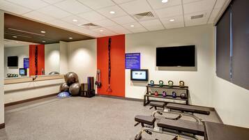 Um centro de fitness com equipamentos de exercício, televisão e espelho.