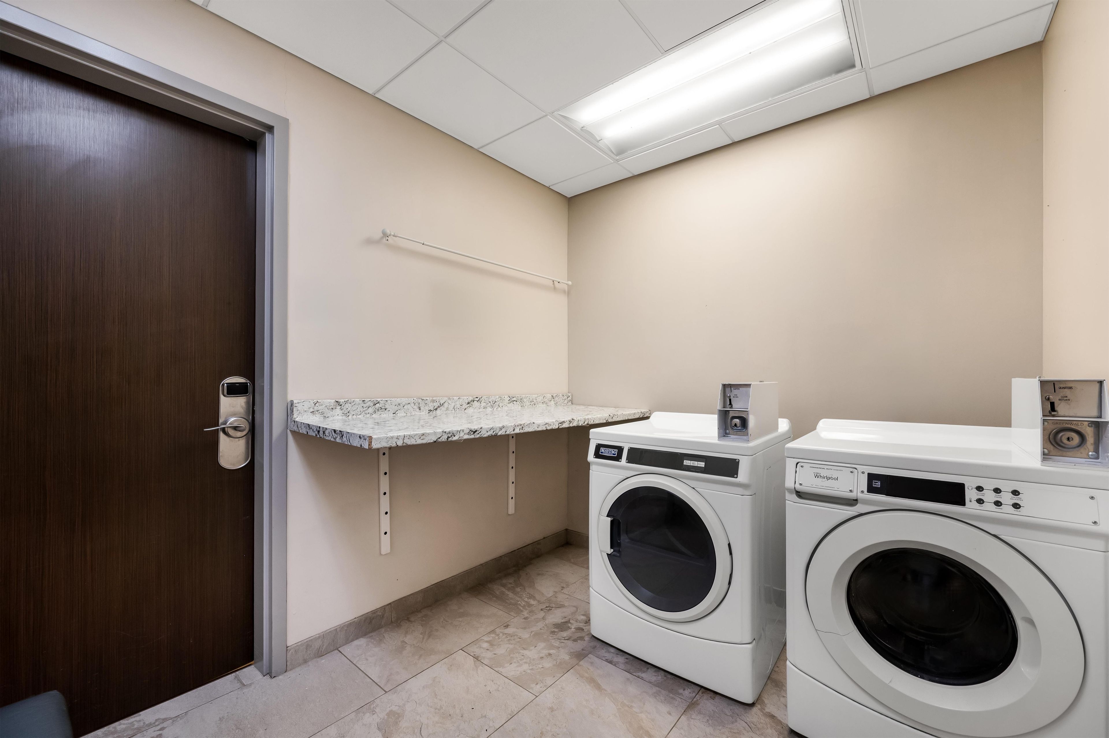 Uma lavanderia com porta, bancada e duas máquinas de lavar roupa.