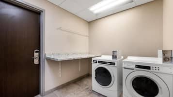 Uma lavanderia com porta, bancada e duas máquinas de lavar roupa.