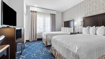 Quarto de hotel com duas camas, uma televisão, uma mesa de escritório e uma janela com cortinas.