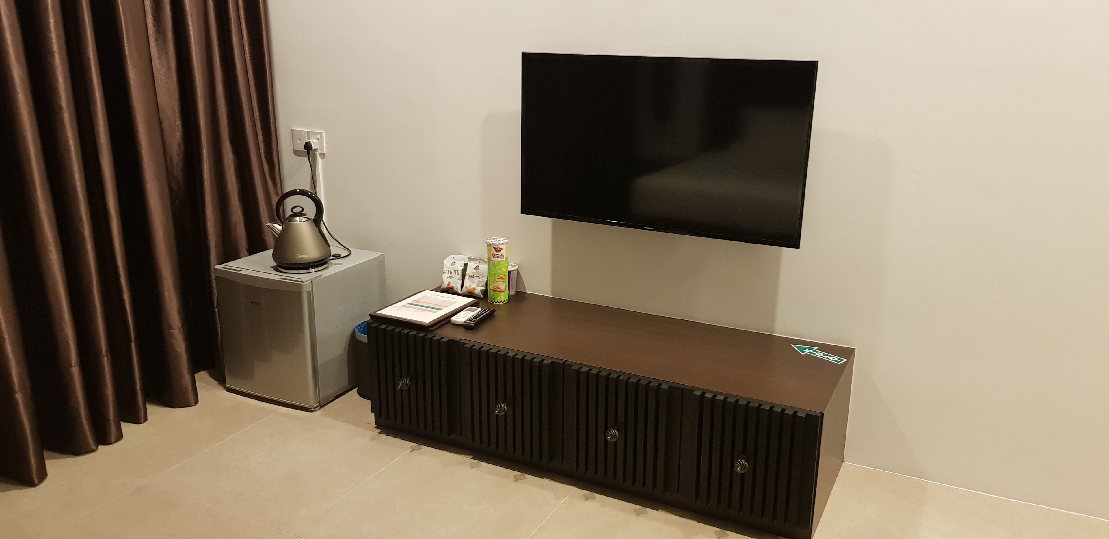 Uma sala de estar moderna com televisão de tela plana na parede, uma mesinha lateral com uma chaleira, um controle remoto e alguns objetos na mesa de centro.