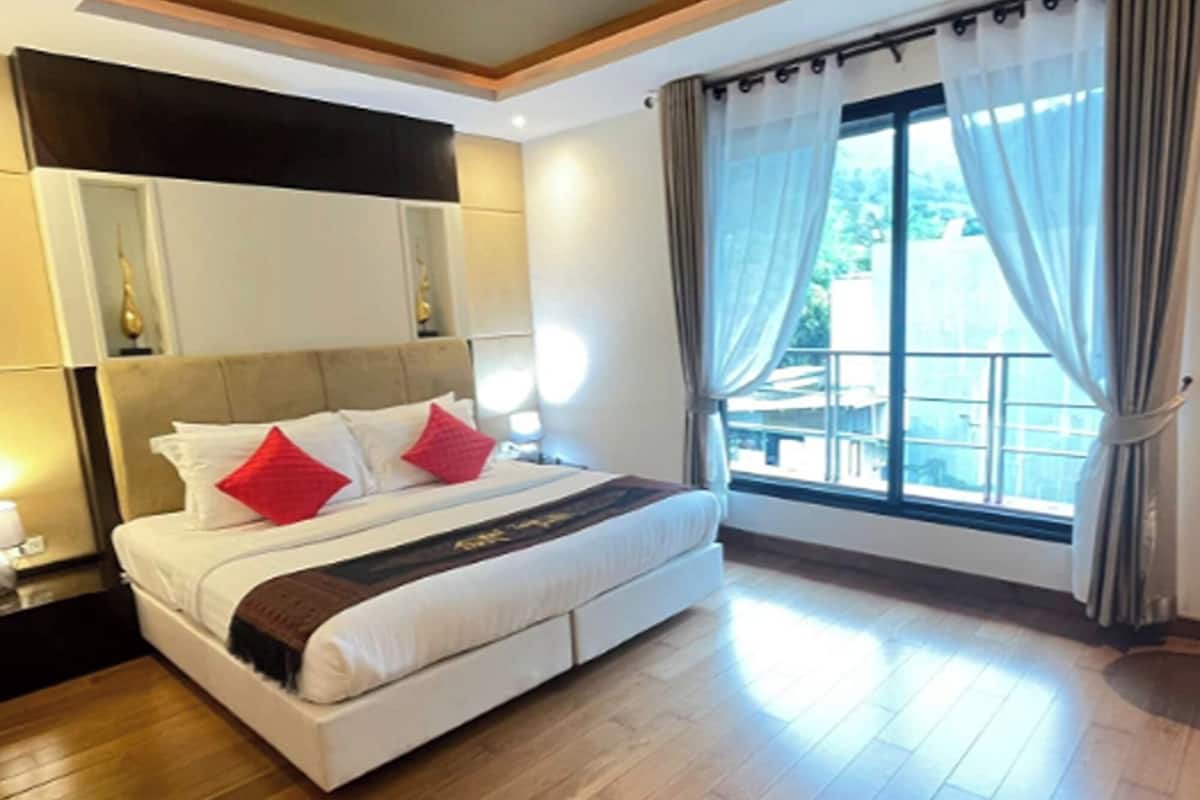 Um quarto espaçoso com uma cama grande, teto com moldura de madeira e uma janela ampla com cortinas.