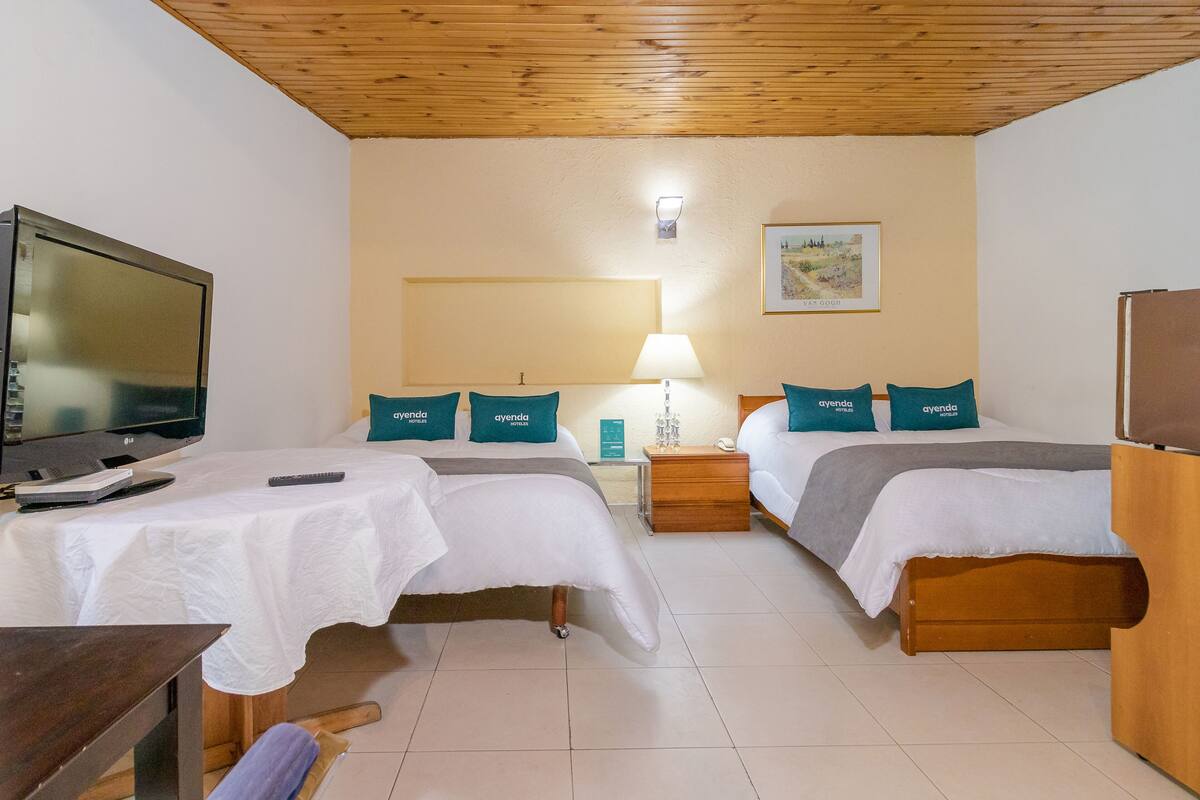 Quarto de hotel com duas camas, uma televisão, um abajur e teto de madeira.