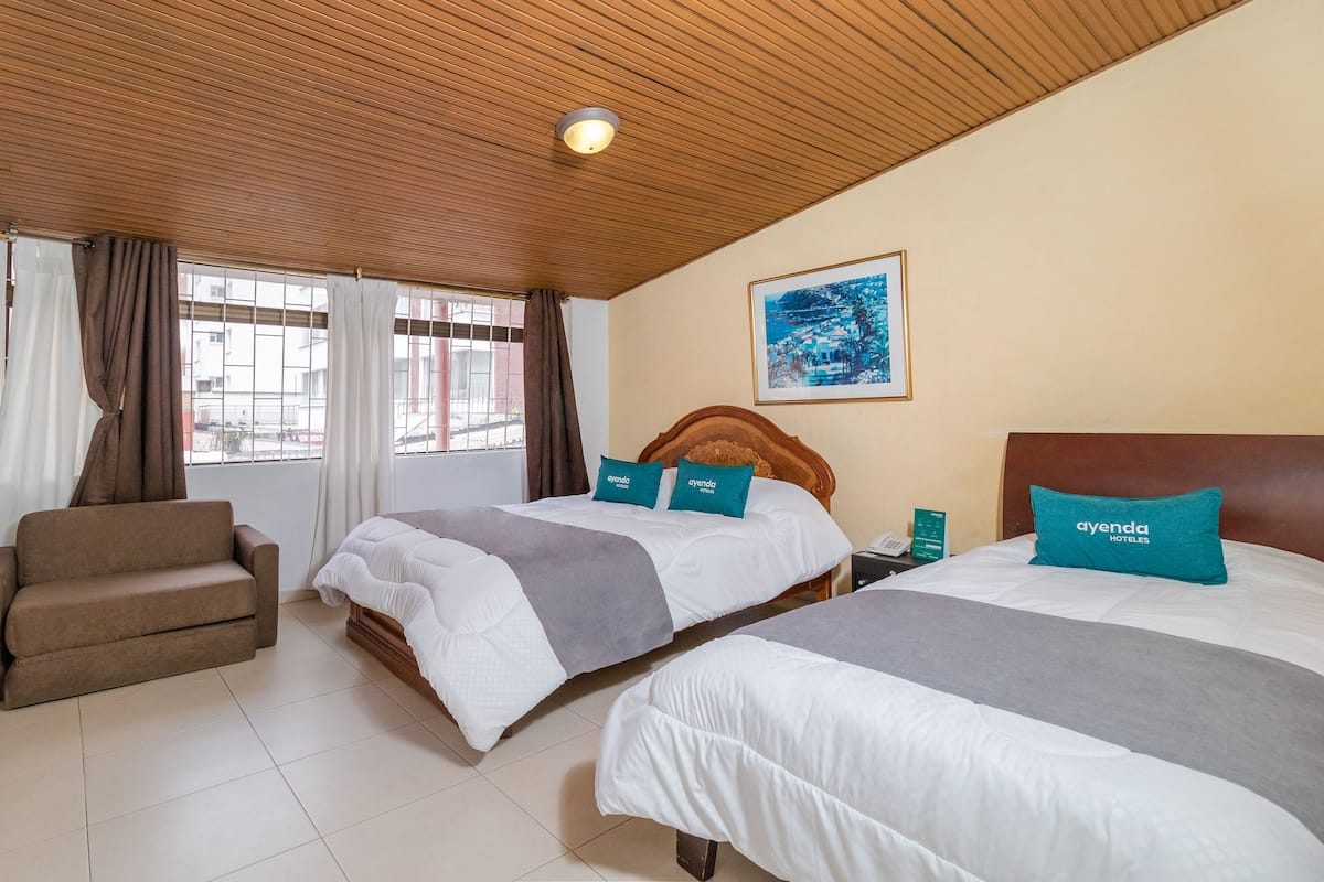 Quarto de hotel com duas camas, um sofá e uma janela com cortinas.