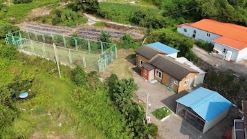 Uma área residencial com um campo esportivo cercado, uma casa com telhado azul e um pequeno galpão.