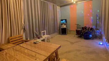 Quarto com uma mesa e cadeiras de madeira, televisão e um kit de bateria.