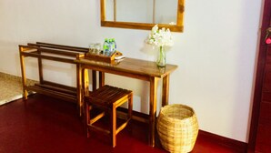 Um console de madeira com um espelho acima, um banquinho pequeno, uma cesta de vime e um vaso com flores brancas.