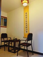 Quarto com uma mesa, duas cadeiras, uma janela e um letreiro fixado na parede com caracteres chineses.