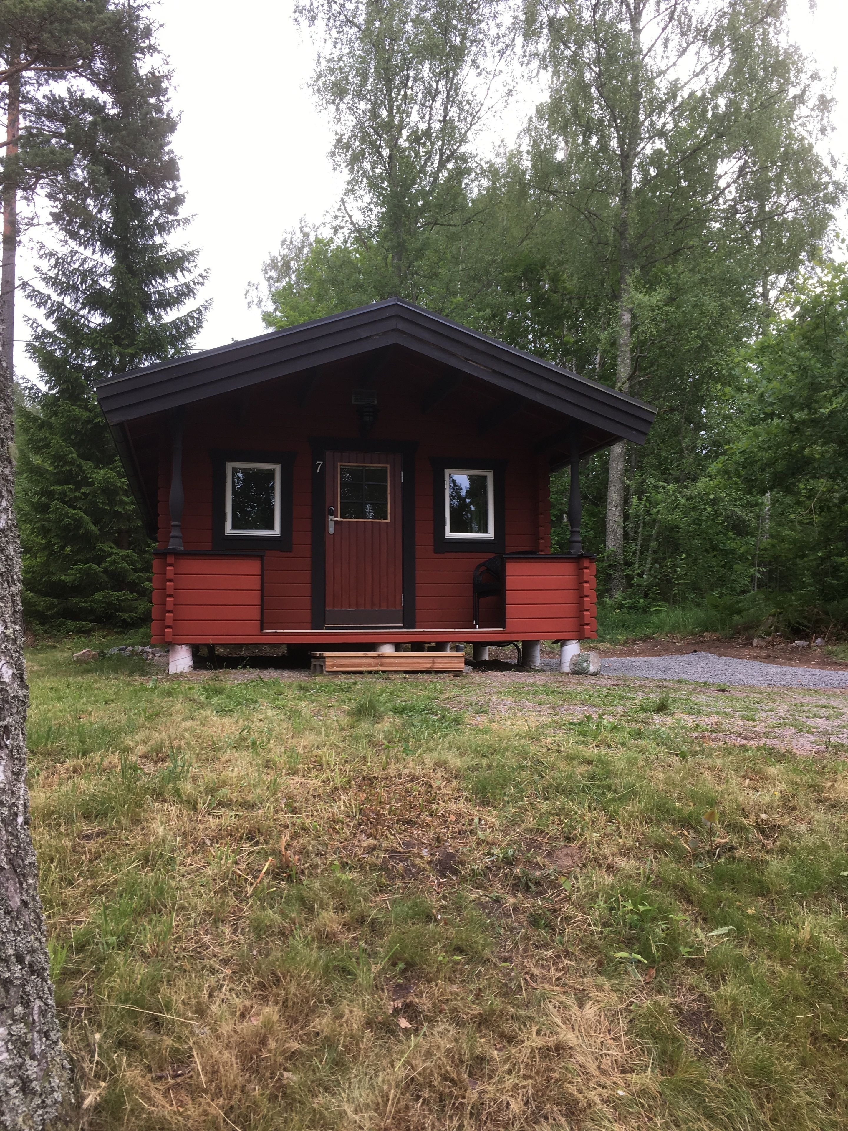 Uma cabana pequena com telhado escuro, uma porta frontal e duas janelas.