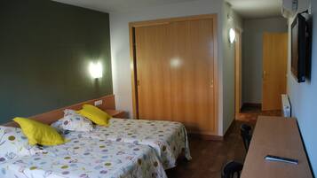 Quarto com duas camas, uma porta de madeira, uma mesa e uma cadeira.