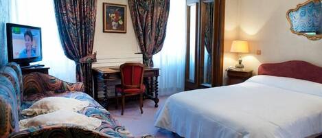 Quarto de hotel com cama, secretária com cadeira, televisão e cortinas.