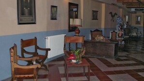 Quarto com duas cadeiras de madeira, uma mesa pequena com um vaso, um radiador e uma parede com quadros emoldurados.