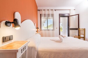 Quarto de hotel com cama, mesa de cabeceira, luminária na parede, janela com cortinas e porta.